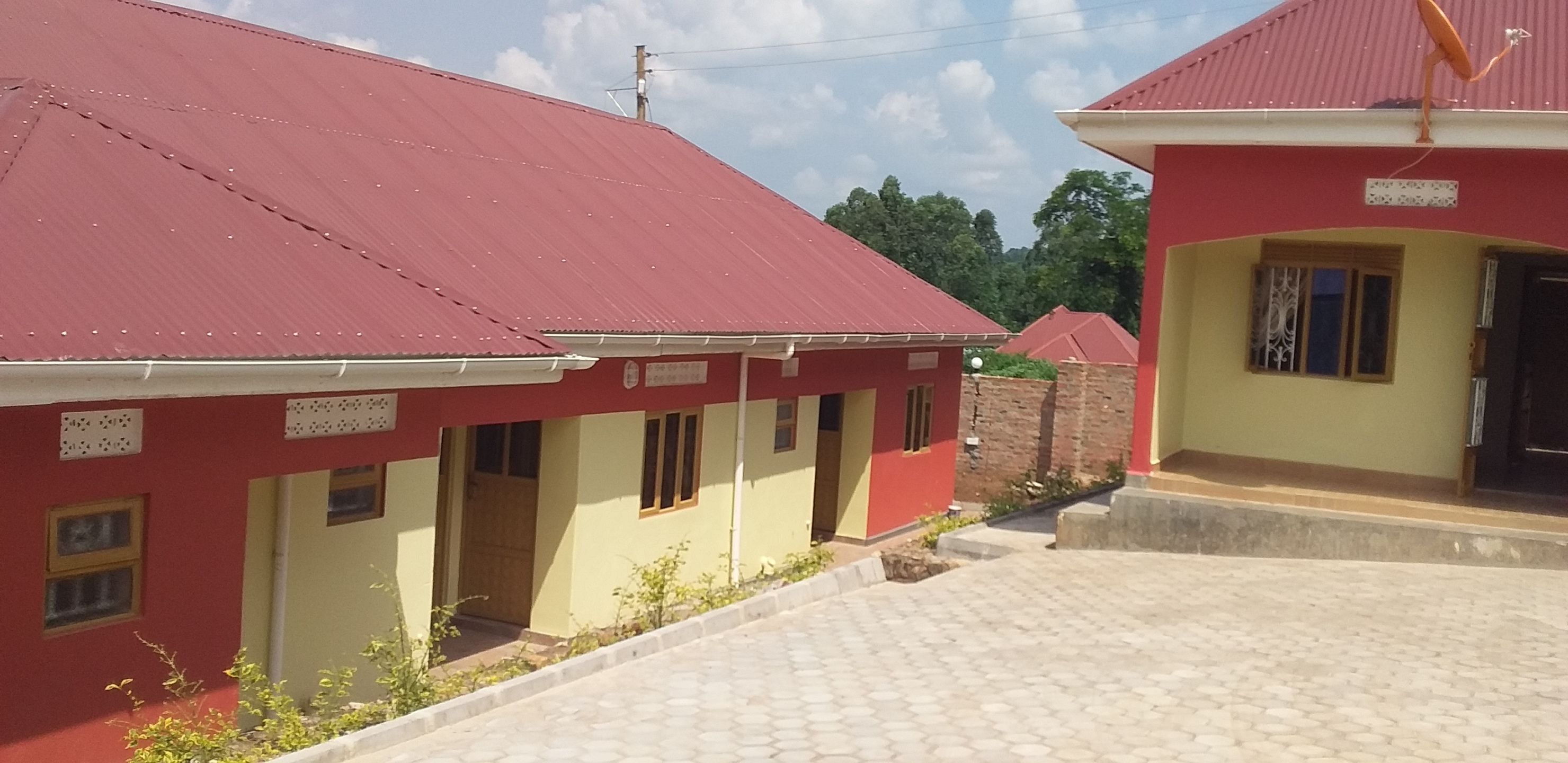 Um edifício com paredes externas em vermelho e amarelo, entrada pavimentada e telhado vermelho.