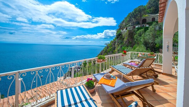 Terraço com vista para o mar, mobiliado com espreguiçadeiras e plantas em vasos.