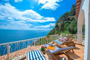 Terraço com vista para o mar, mobiliado com espreguiçadeiras e plantas em vasos.