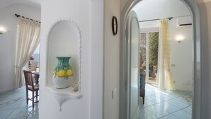Quarto com parede branca, um vaso decorativo com limões, uma cadeira de madeira e vista através de uma porta em arco.