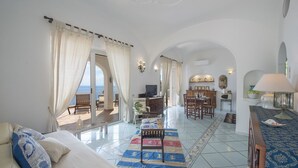 Ampla sala de estar com varanda vista para o mar, área de refeições e cozinha.