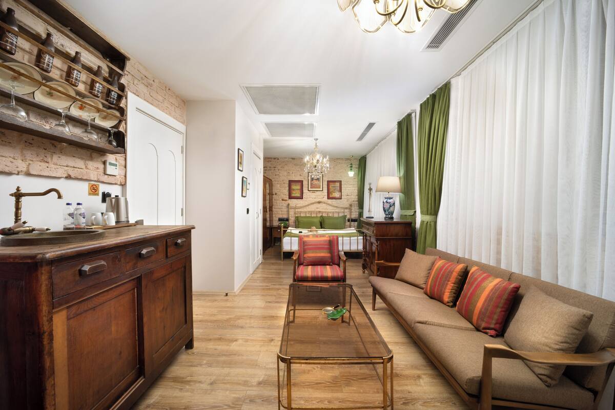 Uma sala de estar com uma mesa de centro de madeira, um sofá com almofadas listradas, uma parede de tijolos e um lustre.