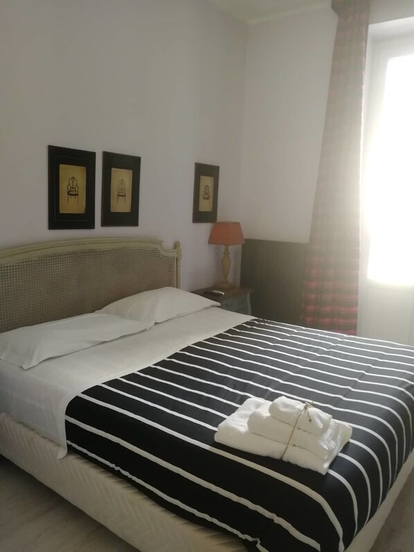 Quarto de hotel com uma cama, cabeceira, mesa de cabeceira, abajur e três quadros na parede.