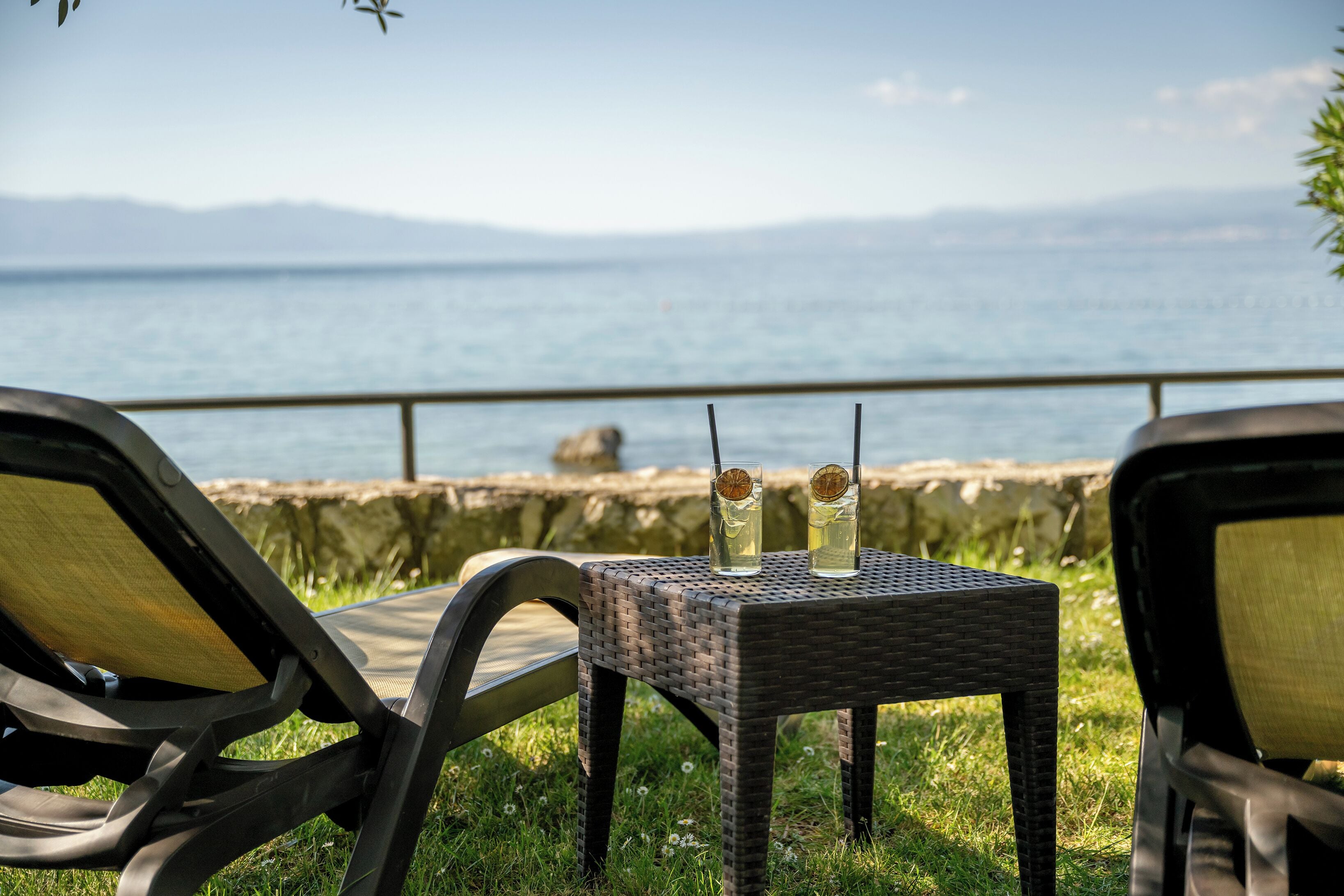 Uma mesa de vime com duas bebidas e vista para o mar.