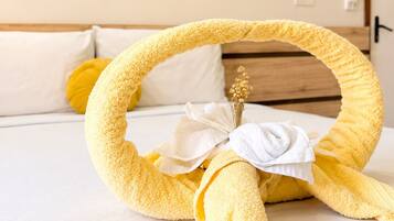 Uma cama bem arrumada com uma toalha disposta em forma circular, um travesseiro branco e um travesseiro amarelo.