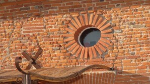 Paredes de tijolos com uma janela circular e uma estrutura metálica que lembra uma vassoura.