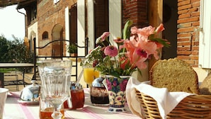Uma mesa de café da manhã com uma cesta de pão, um jarro de vidro, um copo de suco, um pote de geleia e um vaso com flores.