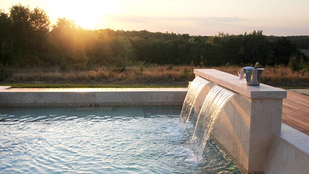 Uma piscina com cachoeira, um balde de metal e um copo na borda.