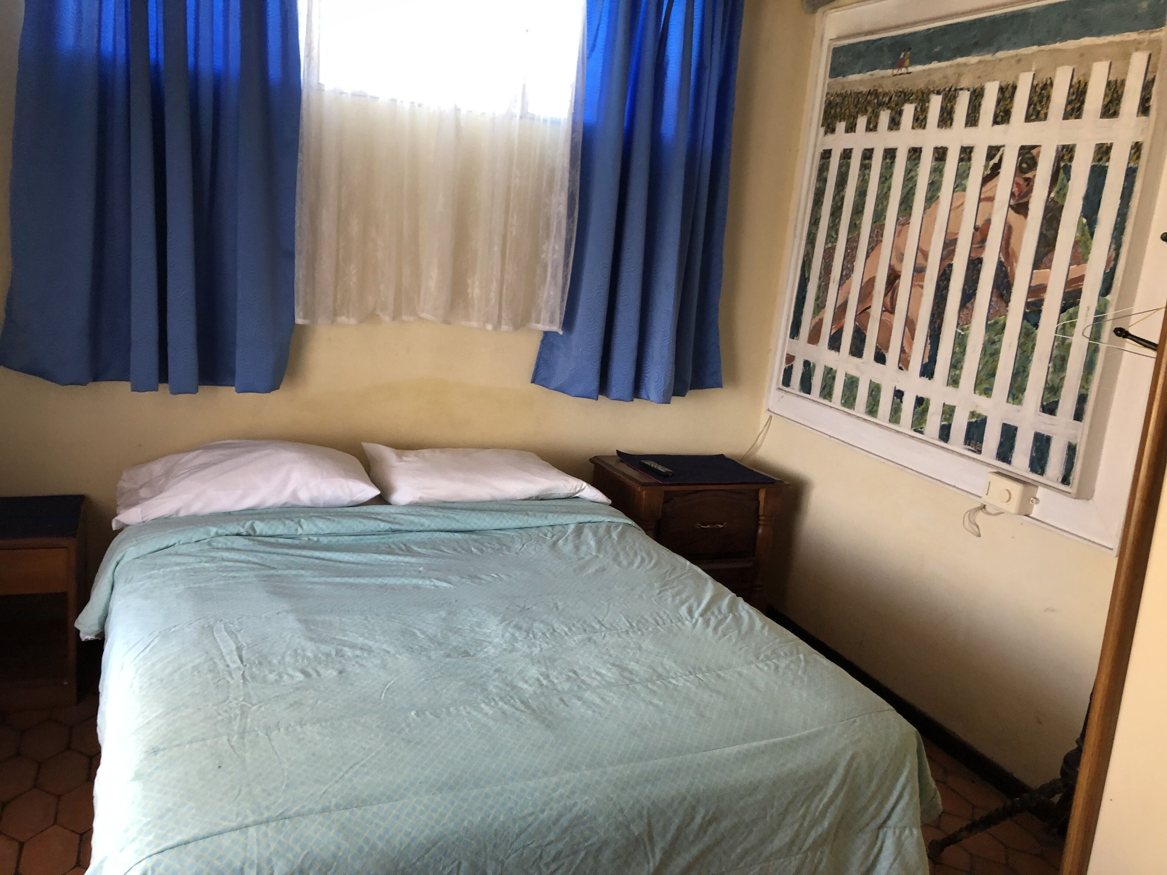 Um quarto com cama, mesa de cabeceira, janela com vista e cortinas.
