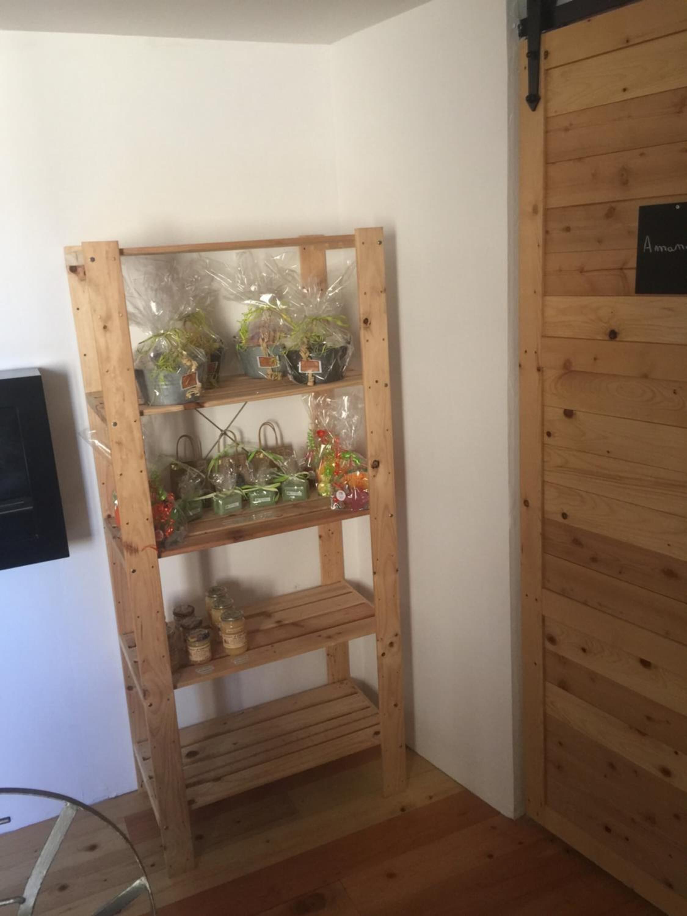 Uma estante de madeira com várias prateleiras, algumas contendo plantas em vasos e outras com potes.