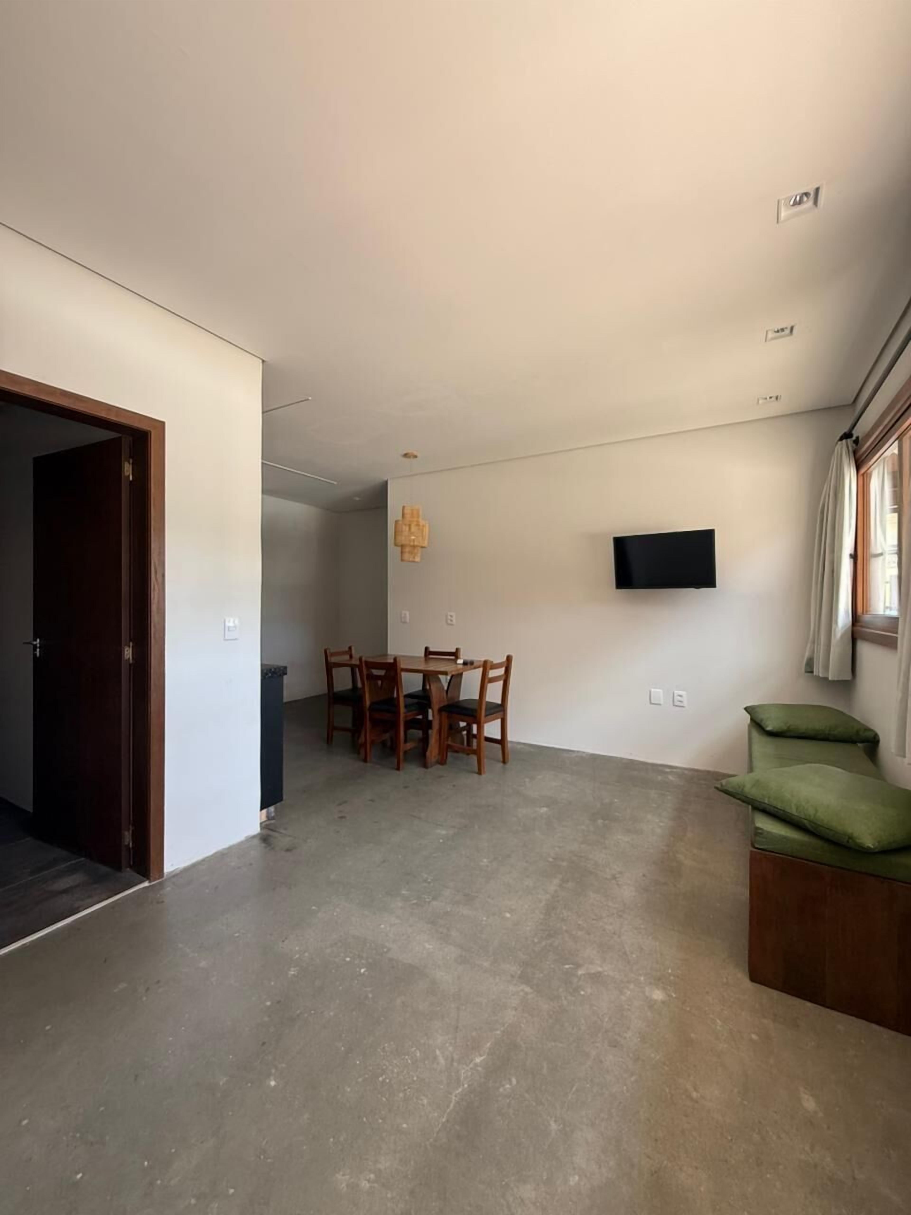 Quarto com uma mesa de jantar e cadeiras, uma TV de tela plana fixada na parede e um banco estofado verde.