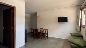 Quarto com uma mesa de jantar e cadeiras, uma TV de tela plana fixada na parede e um banco estofado verde.
