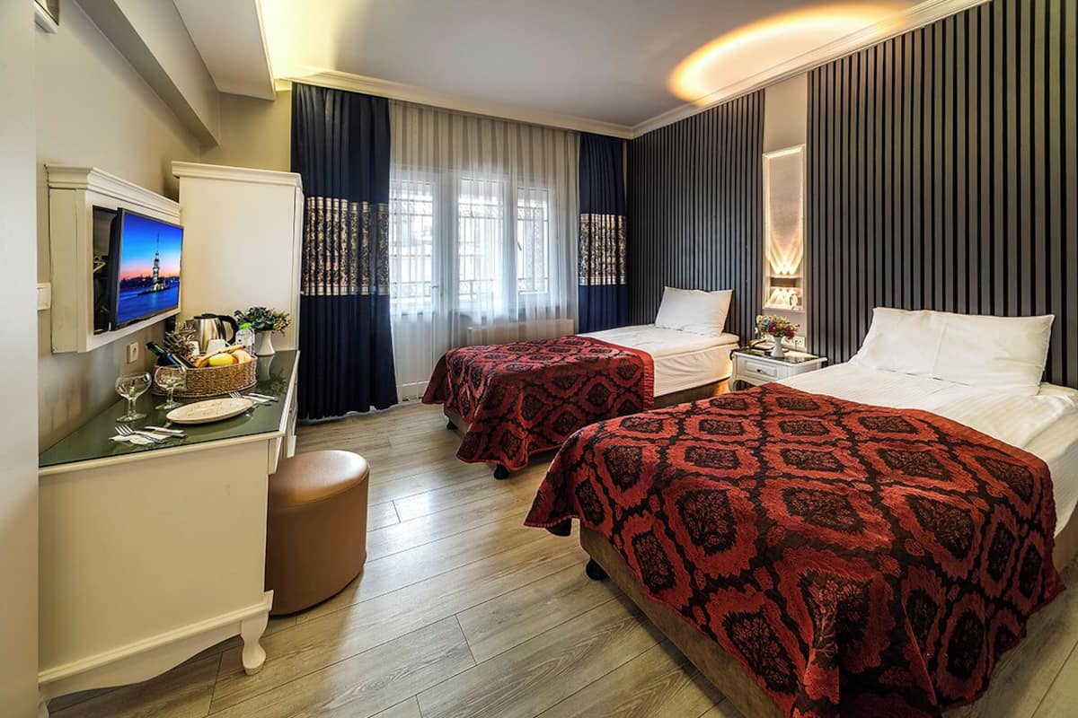Quarto de hotel com duas camas, uma escrivaninha com televisão e um espaço de refeições.