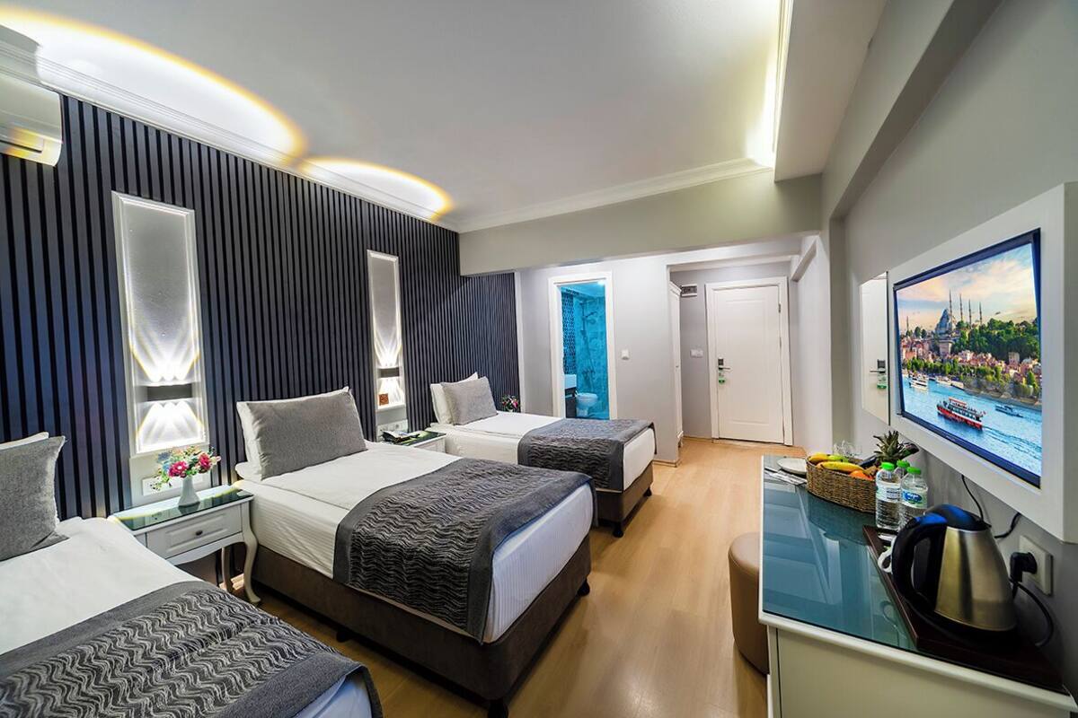 Quarto de hotel com duas camas, uma escrivaninha com televisão e vista para a paisagem urbana.