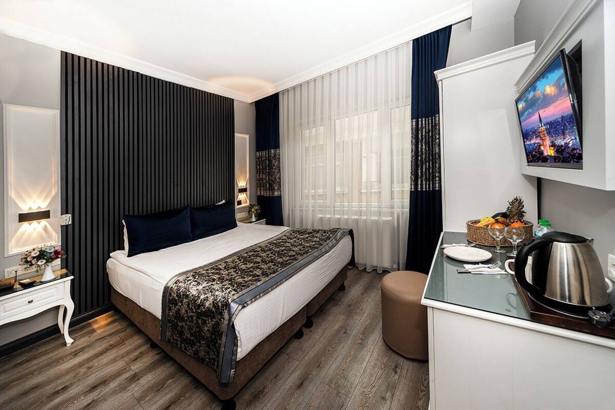 Quarto de hotel moderno com uma cama grande, uma escrivaninha com chaleira e televisão na parede.