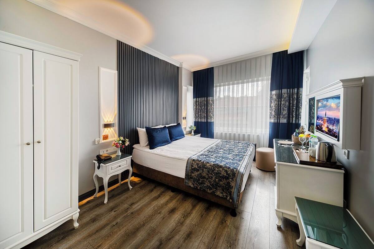 Quarto moderno com uma cama grande, mesa de cabeceira com abajur, cômoda e televisão.