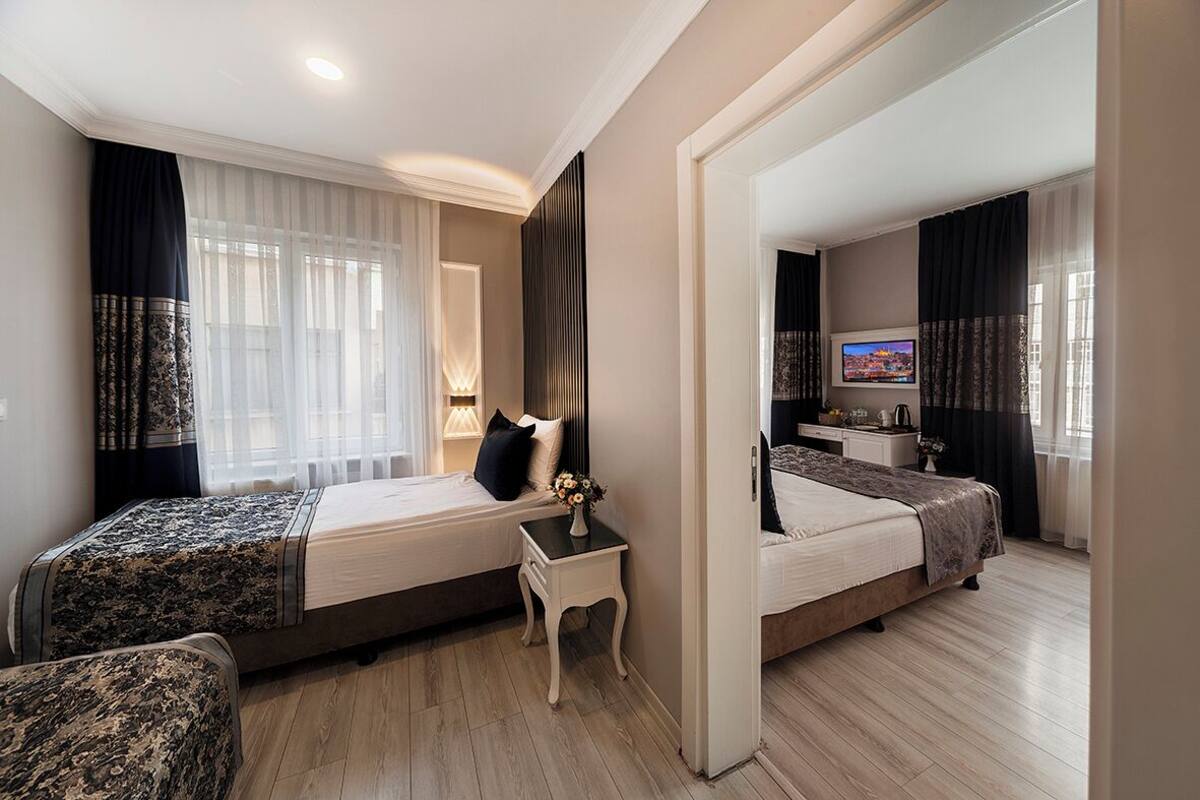 Quarto de hotel com duas camas, televisão, uma mesa pequena com um vaso e um espelho.