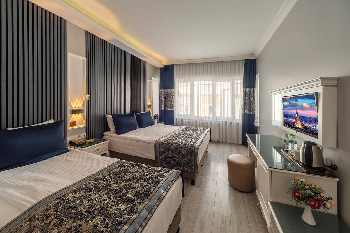 Quarto de hotel com duas camas, uma escrivaninha com televisão e vista para a cidade.