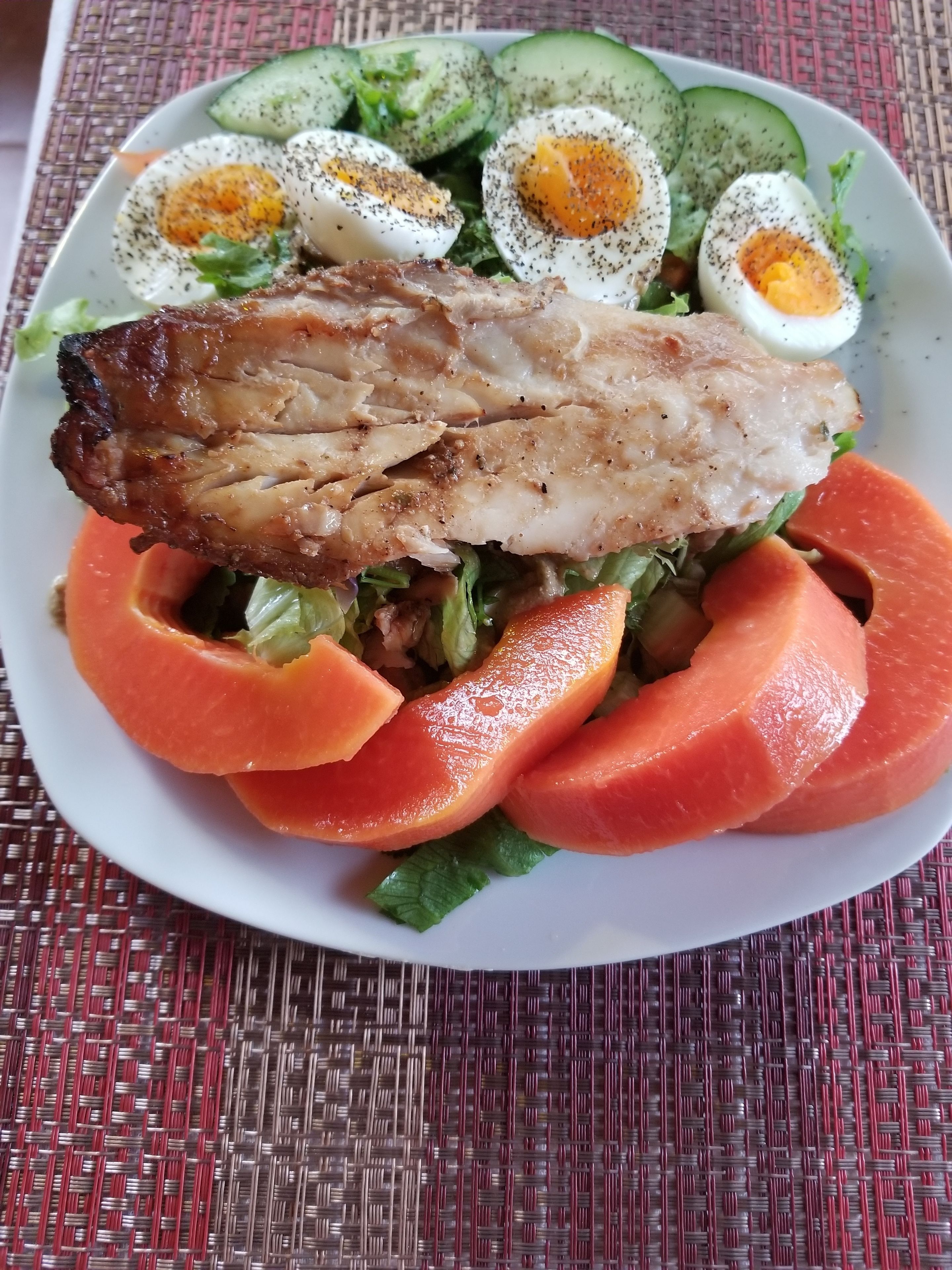 Um prato com carne grelhada, ovos cozidos, fatias de pepino e fatias de cenoura.