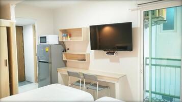 Quarto de hotel compacto com cozinha compacta, televisão de tela plana na parede, cama e varanda com guarda-corpo de vidro.