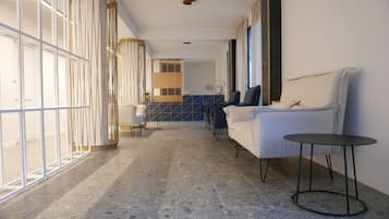 Um lobby moderno de hotel com balcão de recepção, área de estar com sofá e cadeiras, e uma pequena mesa.
