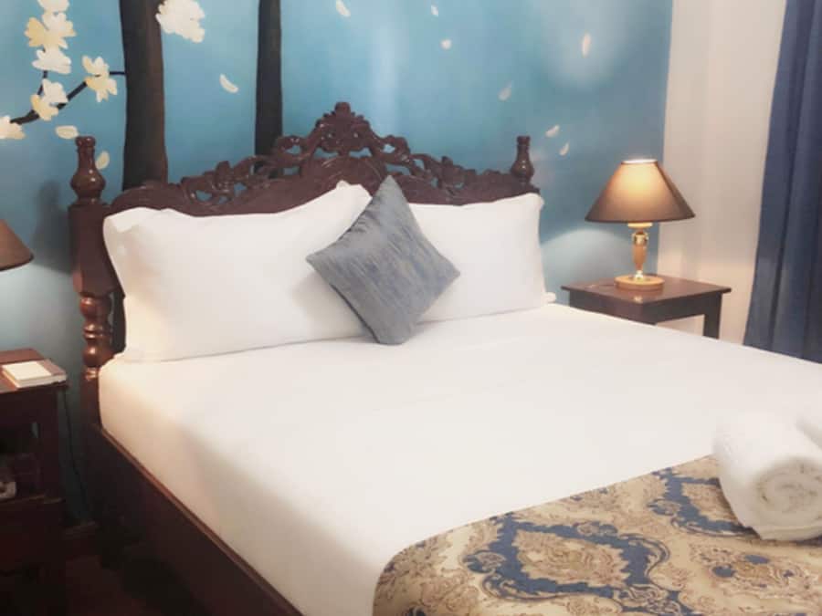 Quarto de hotel com uma cama grande, uma mesa de cabeceira, uma luminária e um mural na parede com tema de árvores e flores.