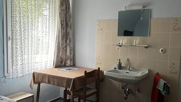 Um quarto com cama, uma mesa com cadeira, pia e janela com cortinas.