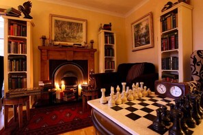 Uma sala de estar aconchegante com lareira, um tabuleiro de xadrez e estantes de livros.