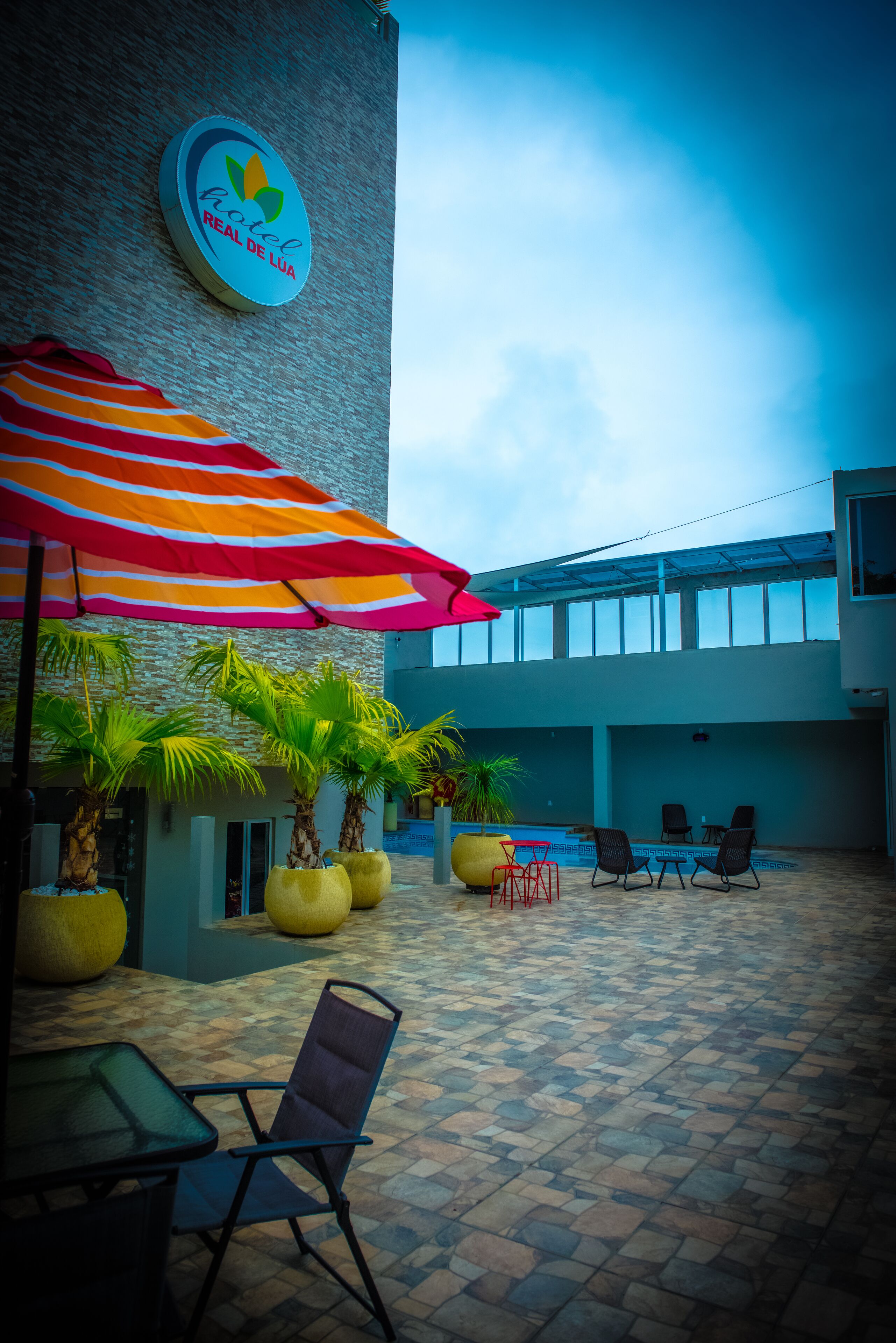 Pátio de hotel com área de estar ao ar livre, palmeiras e piscina.