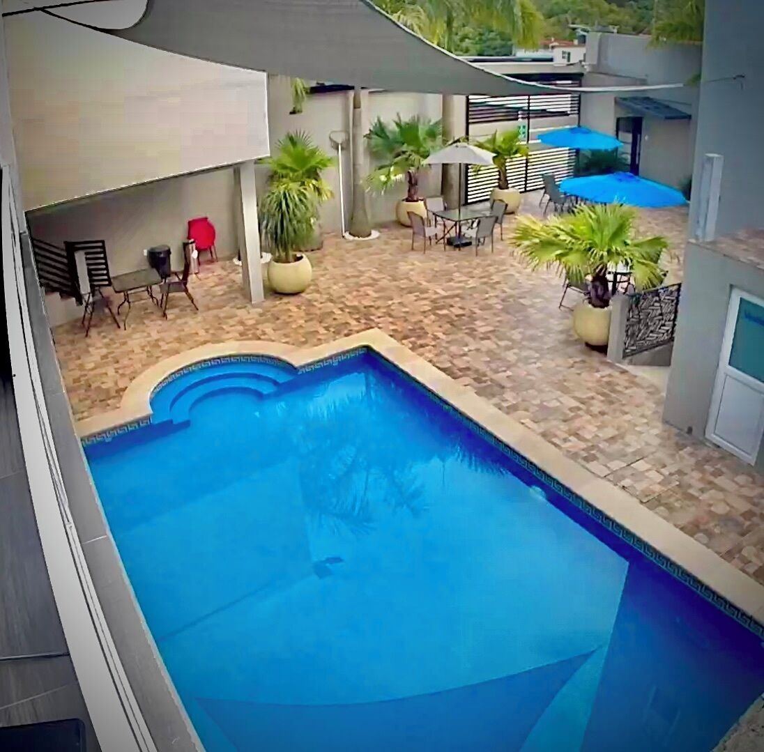 Uma piscina com deck revestido, rodeada por móveis de exterior e plantas em vasos.