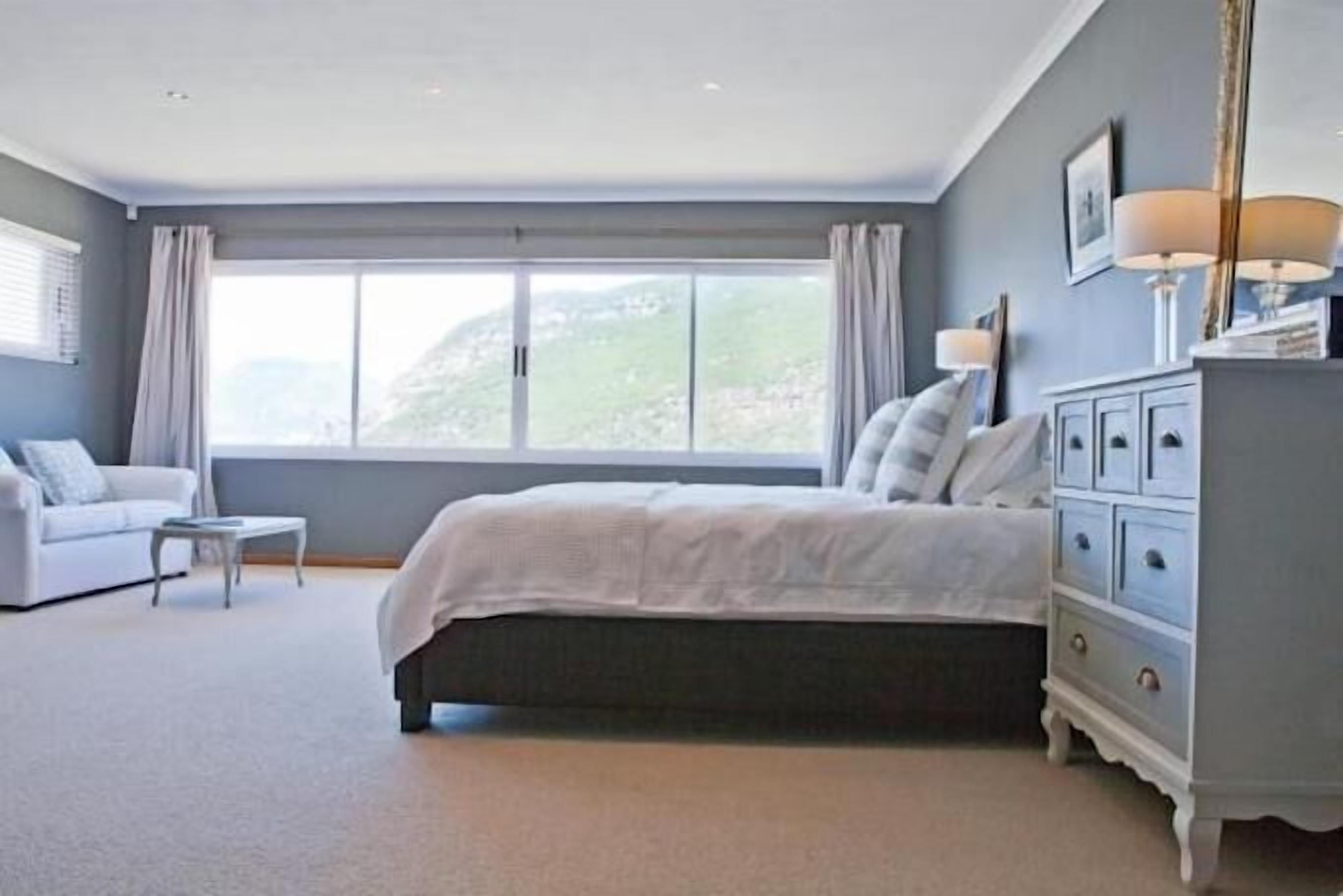 Quarto com uma cama grande, cômoda, mesa de cabeceira e janela com cortinas.
