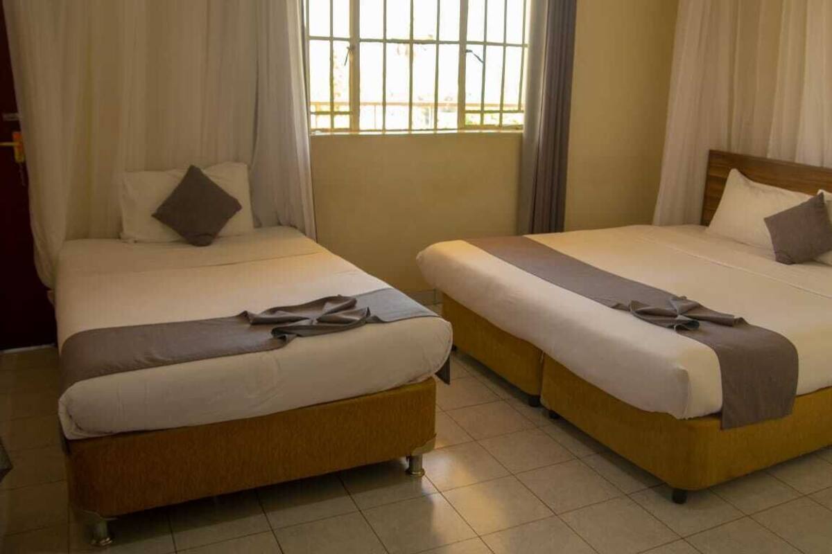 Duas camas de solteiro com estrutura de madeira e roupa de cama branca, uma janela com grades e cortinas.