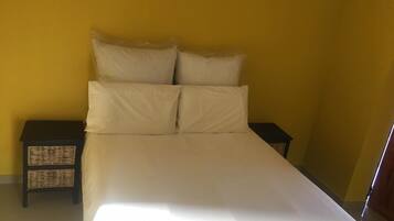 Uma cama com roupa de cama branca num quarto com paredes amarelas.