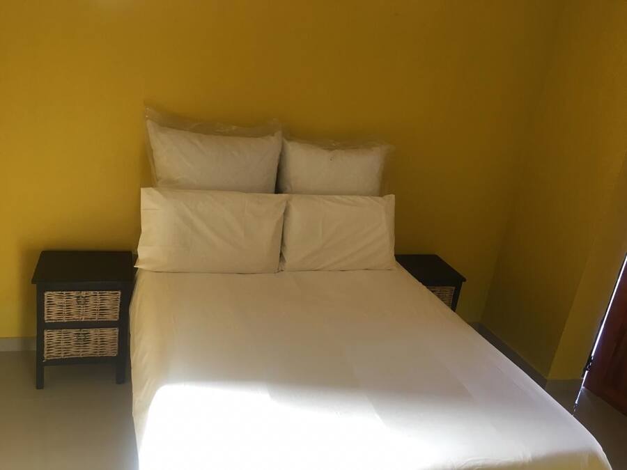 Uma cama com roupa de cama branca num quarto com paredes amarelas.