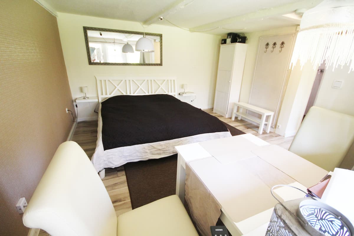 Um quarto com cama, escrivaninha, cadeira, guarda-roupa e espelho.