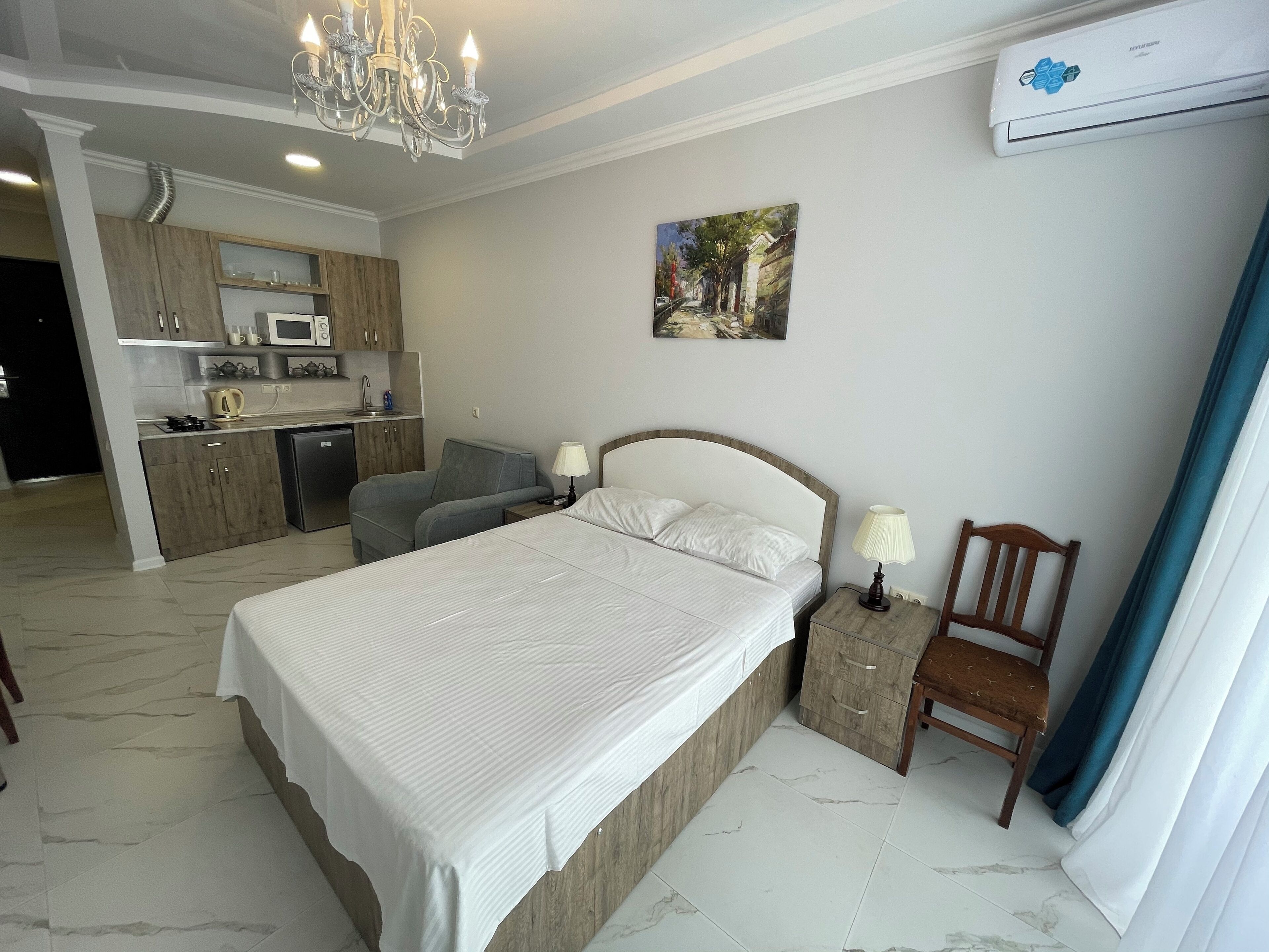 Quarto de hotel com cama, mesas de cabeceira, uma cadeira, escrivaninha, cozinha compacta e ar condicionado.