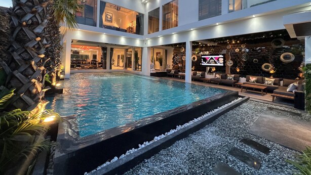 Uma área moderna à beira da piscina, com uma piscina grande, assentos externos e uma entrada bem iluminada.