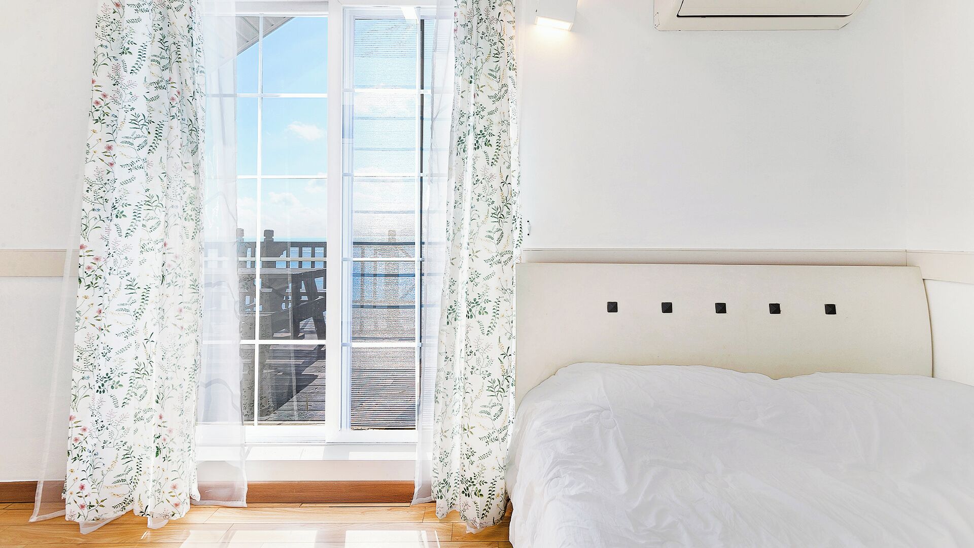 Quarto com uma janela grande, uma cama com cabeceira e vista para edifícios.