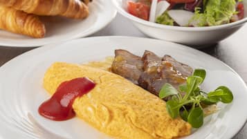 Um prato com omelete, carne e vegetais, e uma saladeira com tomates e vegetais ao fundo.