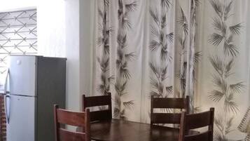 Uma sala de jantar com uma mesa e quatro cadeiras, uma geladeira e uma cortina estampada.