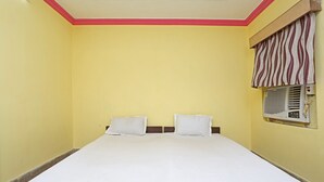 Quarto com uma cama de solteiro, duas almofadas, uma janela com cortina listrada e um aparelho de ar condicionado.