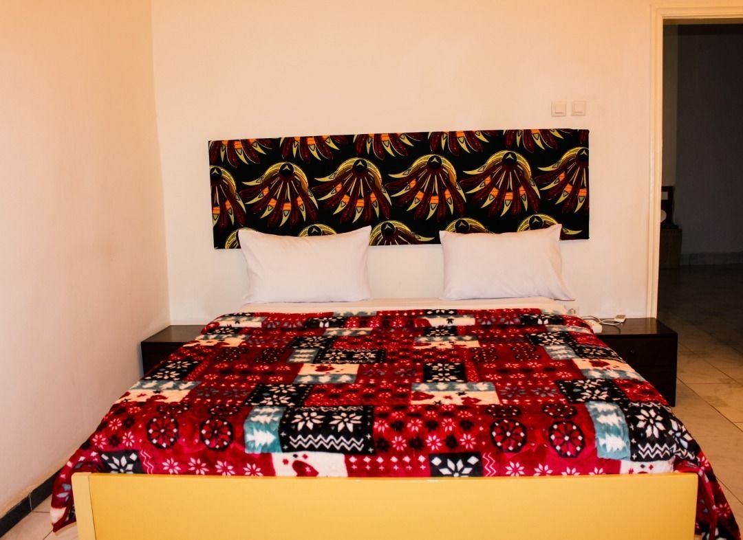 Uma cama com cabeceira estampada, colcha vermelha e preta e travesseiros brancos.