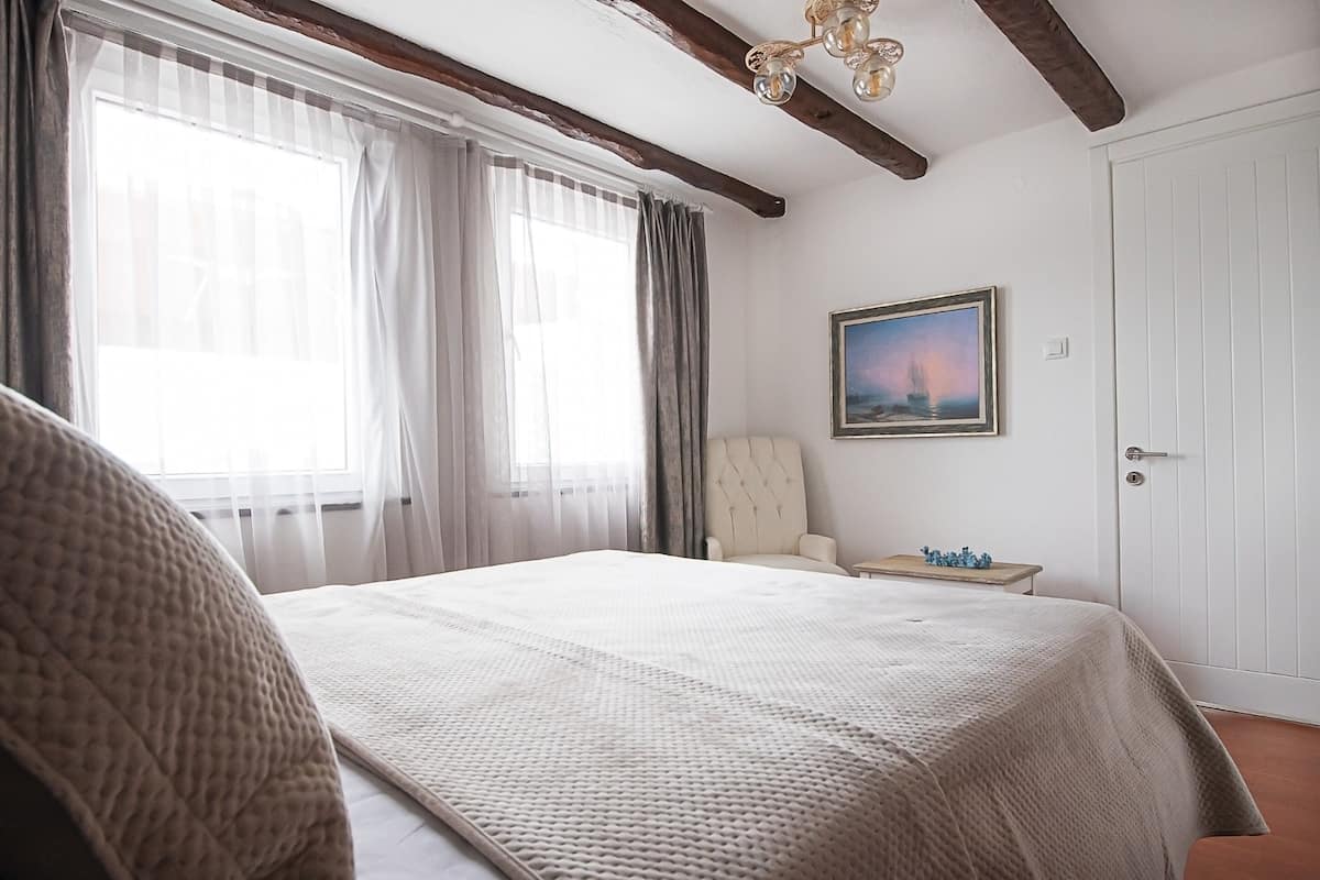 Quarto com uma cama grande, uma cadeira, uma mesa pequena, um quadro e uma porta.
