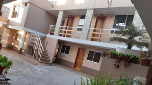 Um edifício residencial de vários andares com uma escadaria que leva ao andar superior, plantas em vasos e uma palmeira.