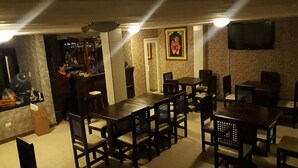 Uma área de refeições com parede de tijolos, uma televisão fixada na parede e um bar com prateleiras e garrafas.