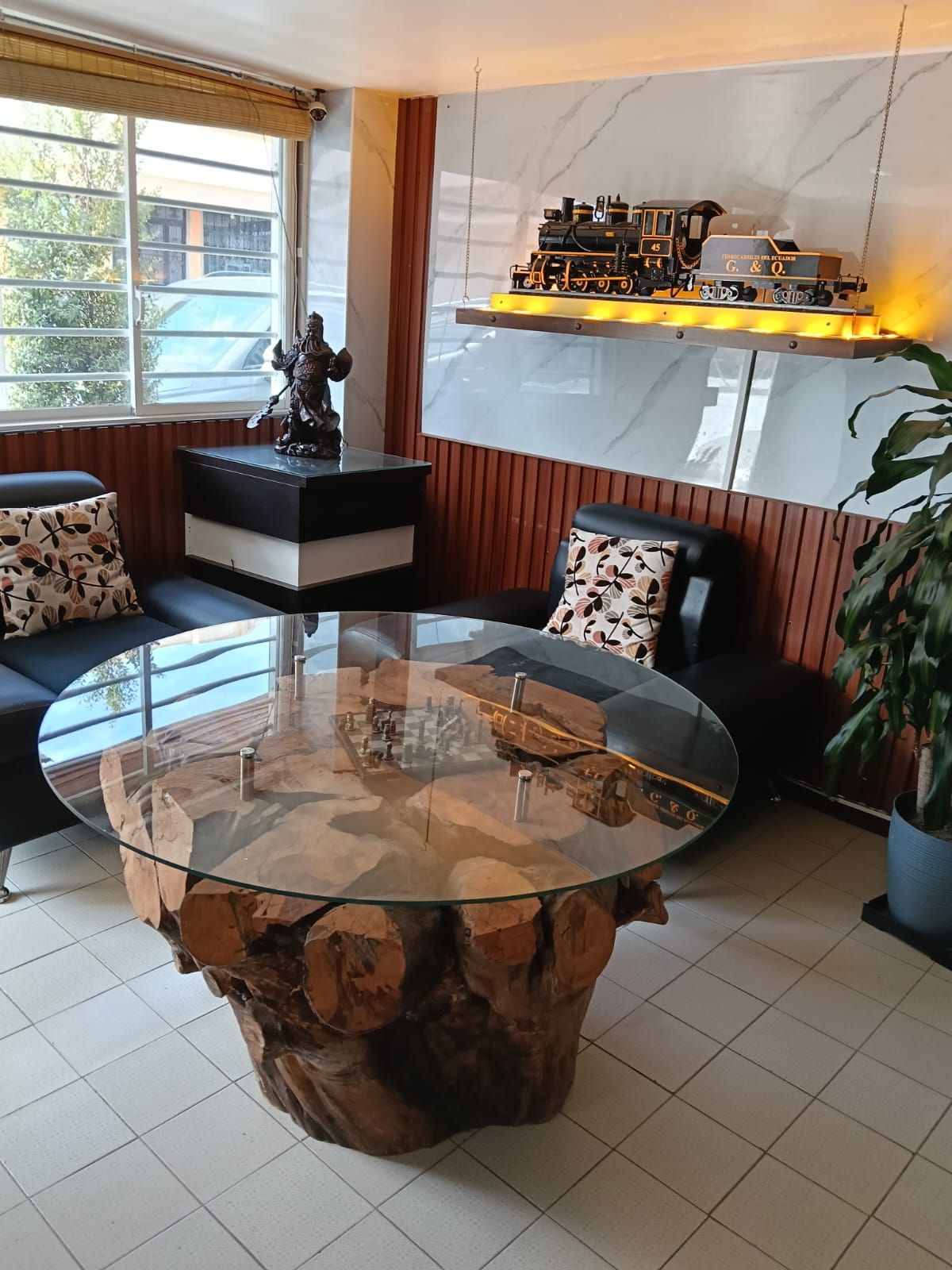 Uma sala de estar moderna com uma mesa de centro de vidro, um sofá e uma estante decorativa com um modelo de trem.