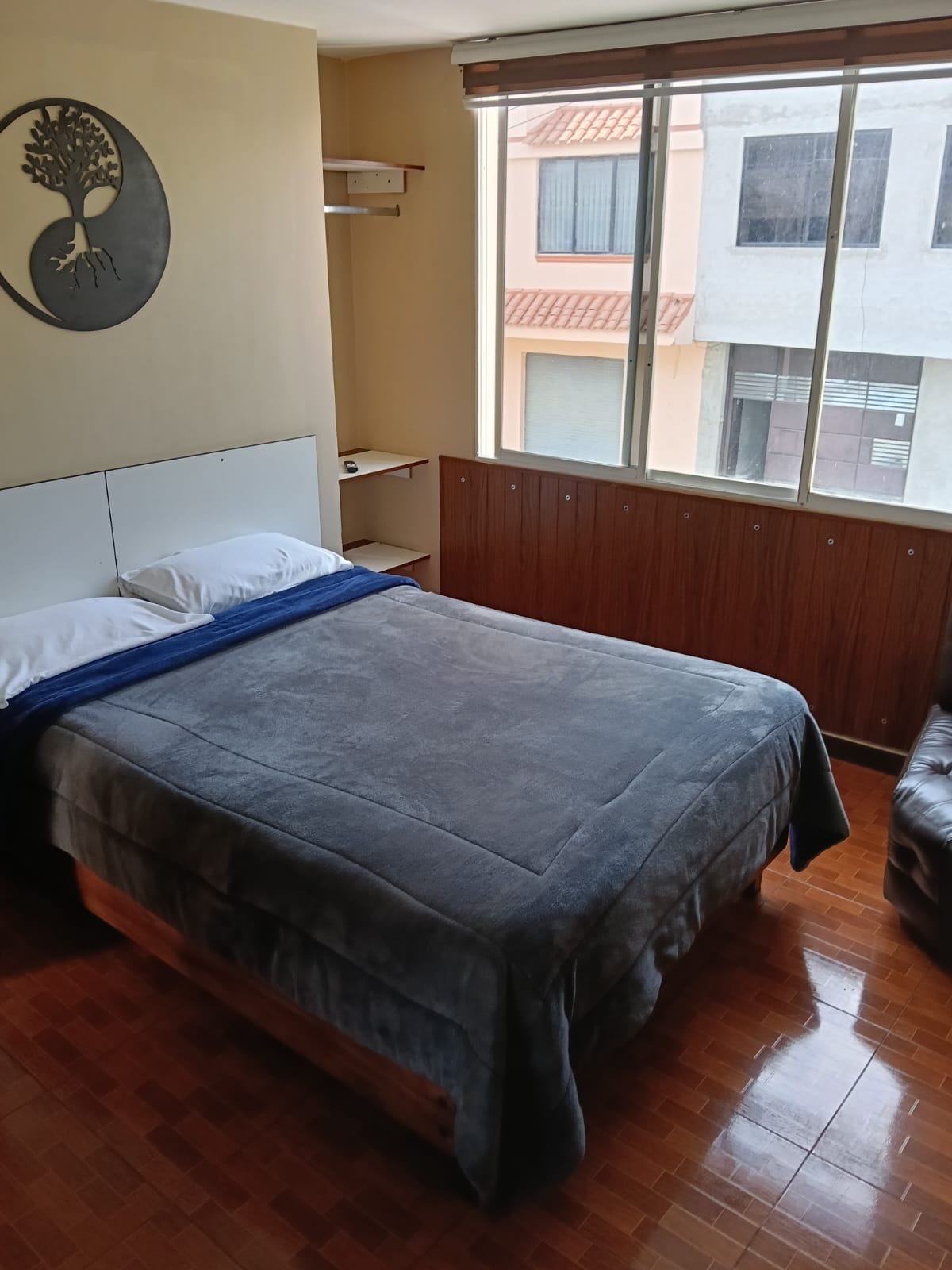 Quarto com cama, cabeceira de madeira, janela e um objeto decorativo na parede.