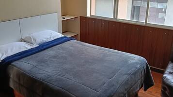 Quarto com cama, cabeceira de madeira, janela e um objeto decorativo na parede.