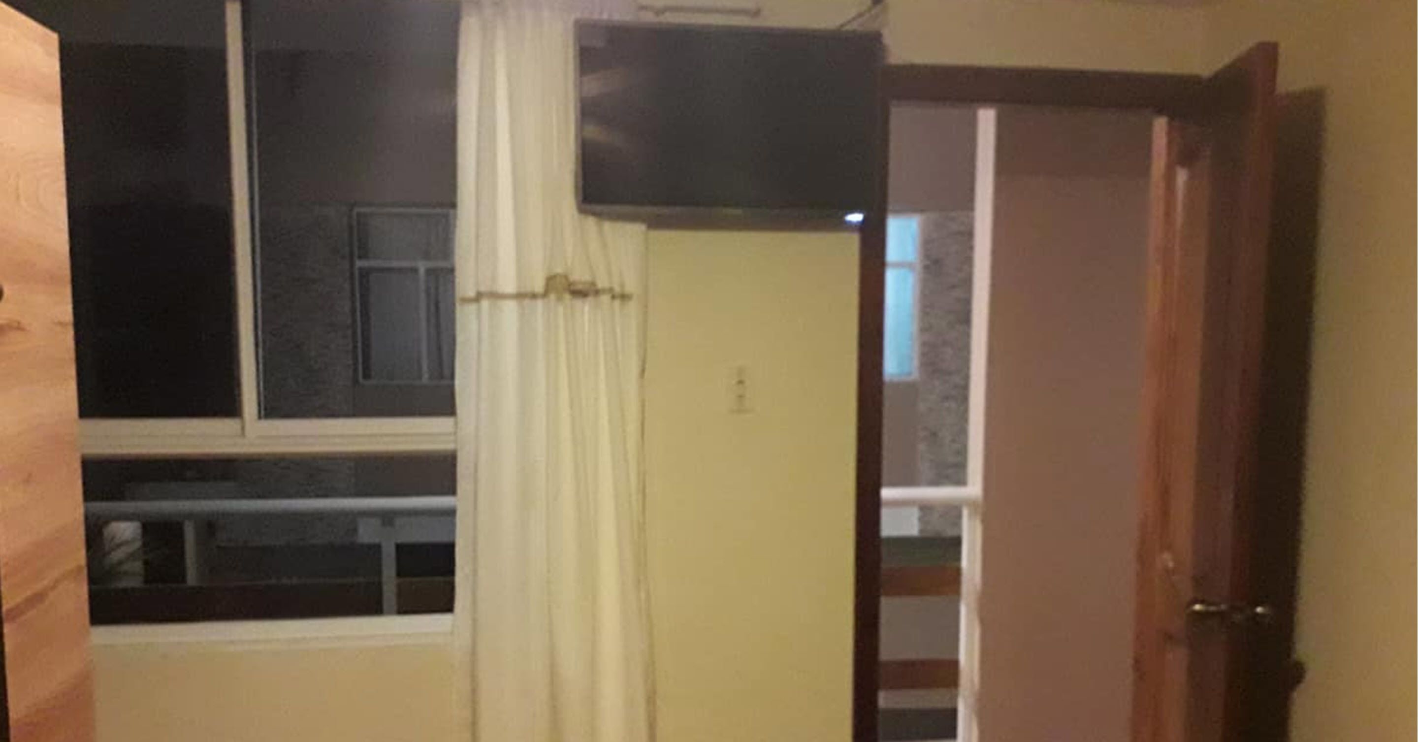 Um quarto com janela, porta e televis ão fixada na parede.