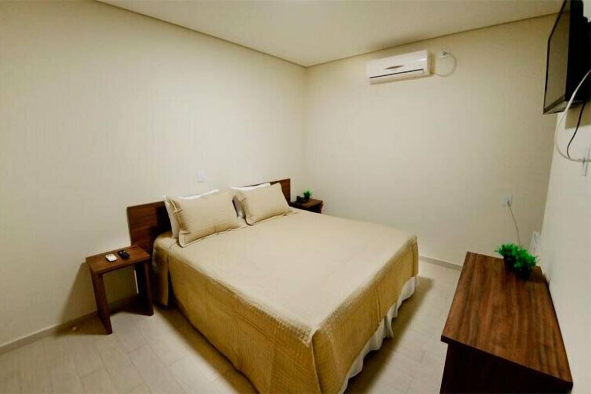 Quarto com cama, mesas de cabeceira, televisão e uma pequena mesa com uma planta.